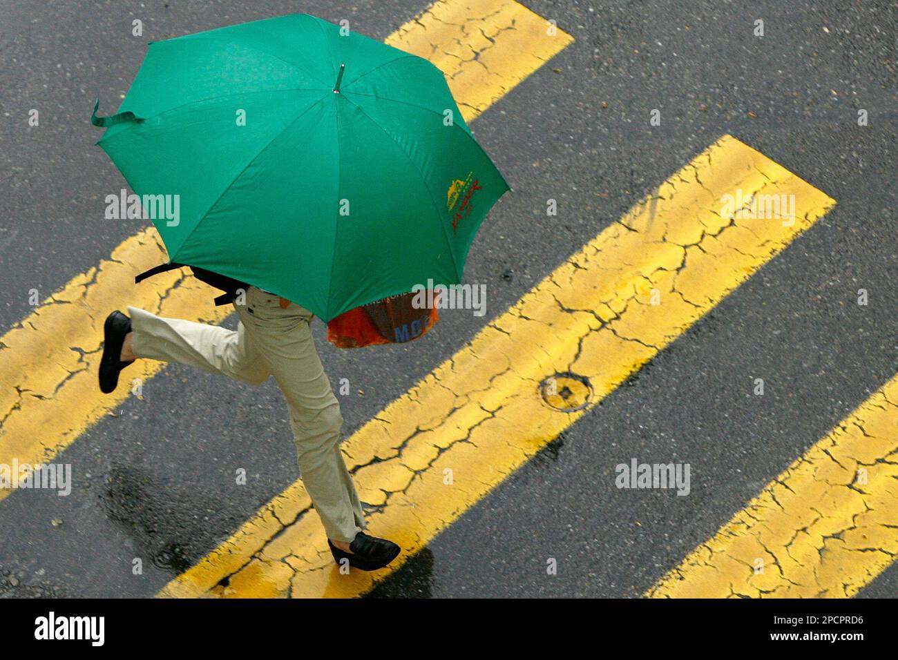 Ein Mann mit Regenschirm rennt ueber einen Fussgaengerstreifen waehrend ...