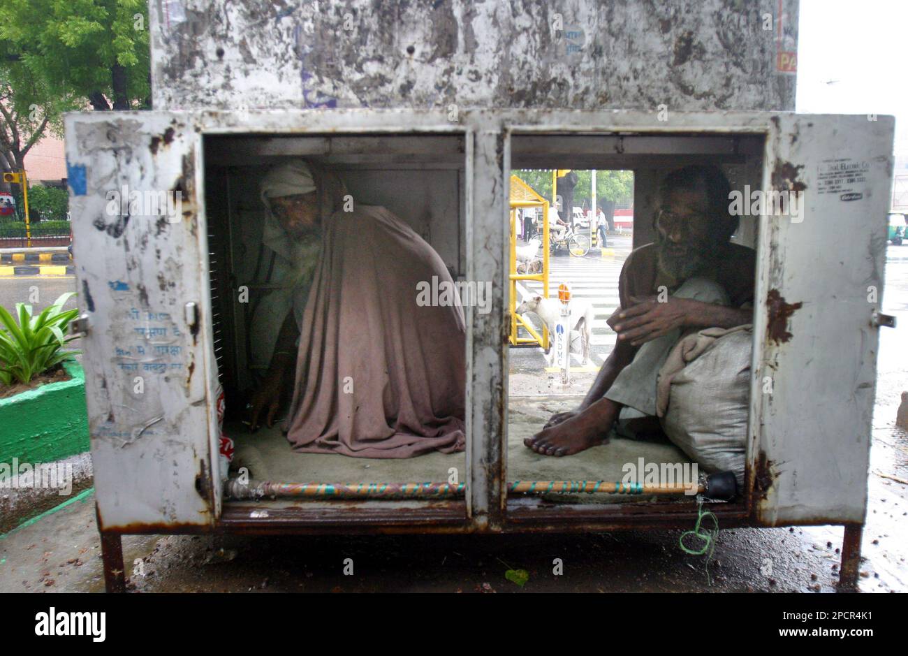 Two homeless men take shelter from the rain at a traffic kiosk in New ...