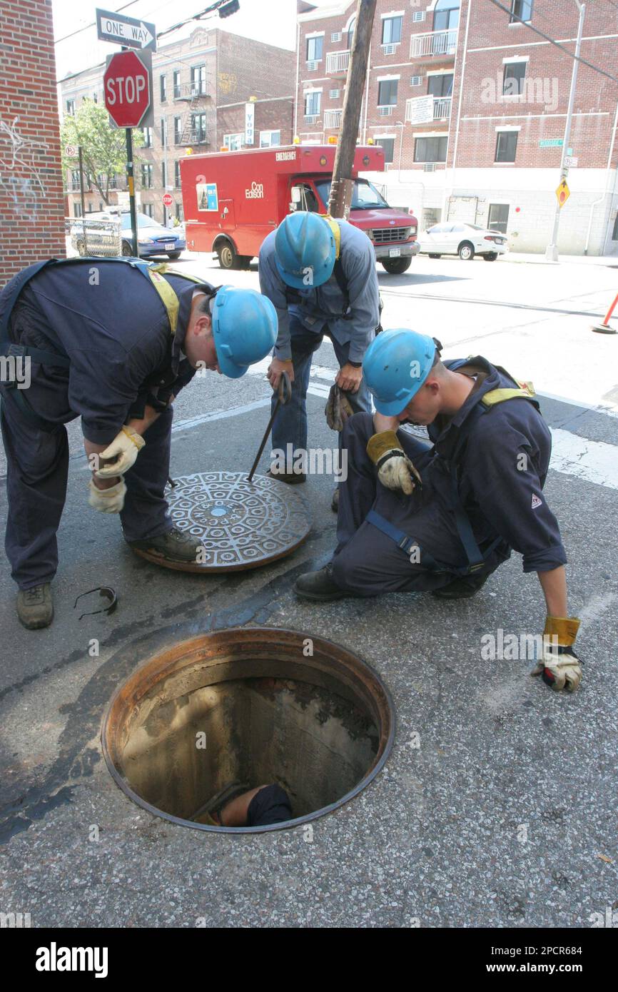 Con Edison workers stand by as a fellow worker checks inside a manhole ...