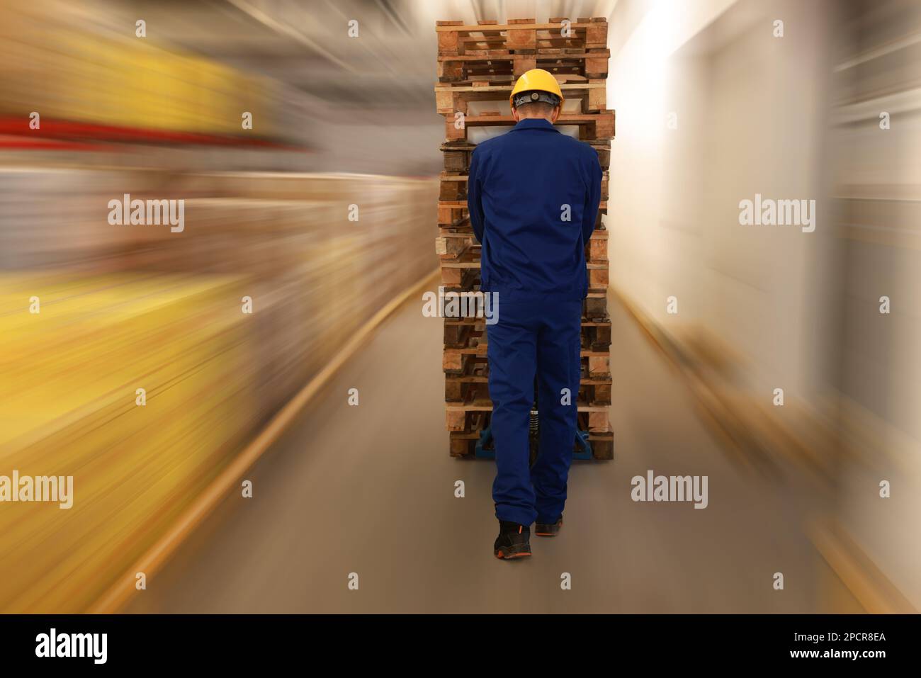 Worker moving wooden pallets with manual forklift in warehouse, back ...