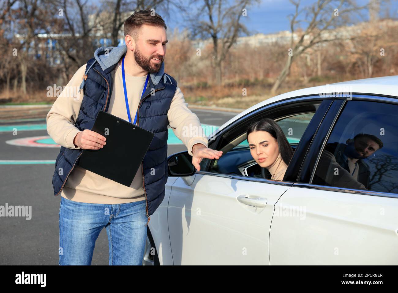 Instructor near car with young woman during exam on test track. Driving ...