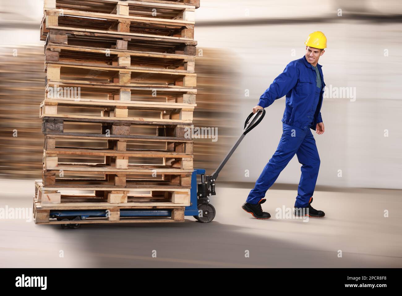 Worker moving wooden pallets with manual forklift in warehouse Stock ...