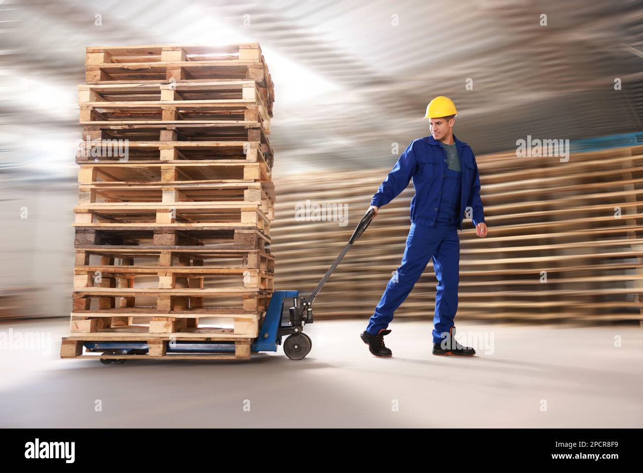 Worker moving wooden pallets with manual forklift in warehouse Stock ...
