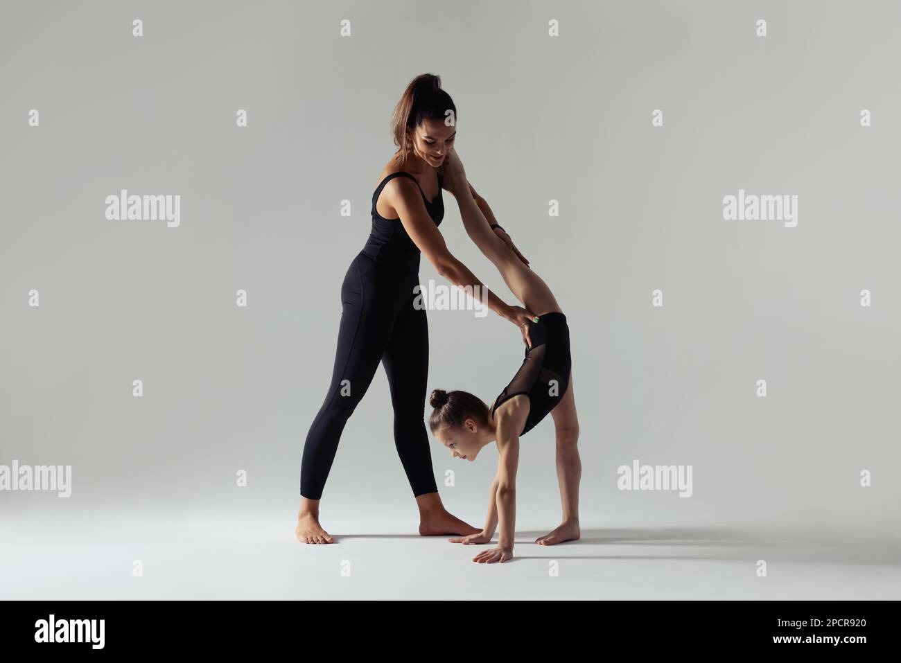 Gymnastic coach helping little girl to do split on white background ...