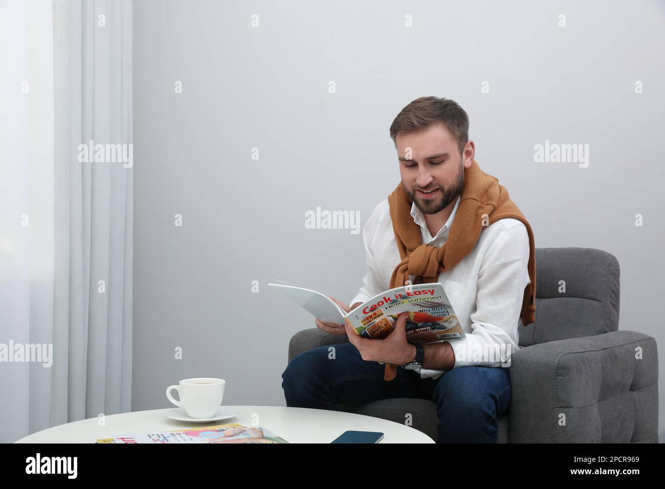 Handsome man reading magazine in armchair at home Stock Photo - Alamy