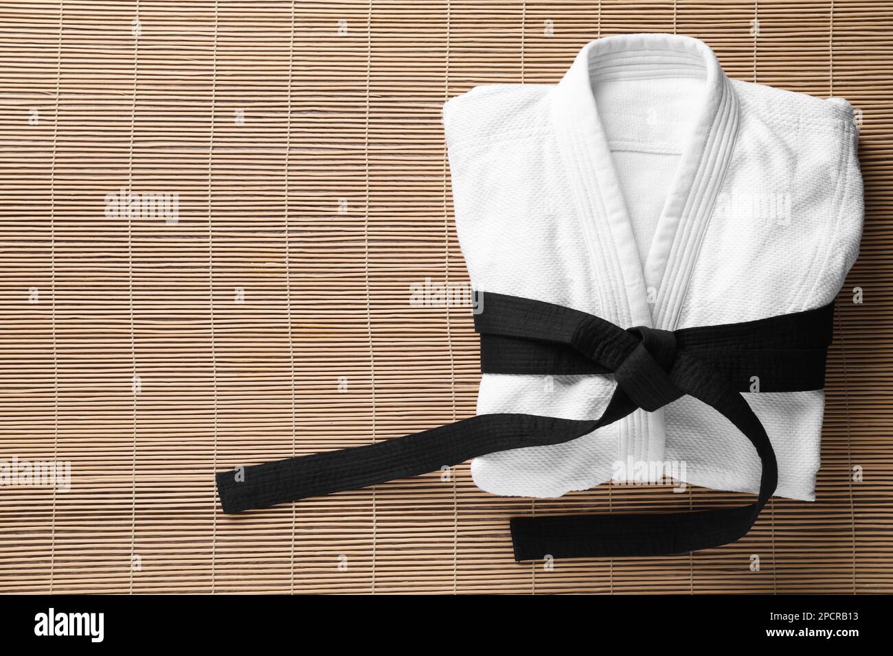 Martial arts uniform with black belt on bamboo mat, top view. Space for ...