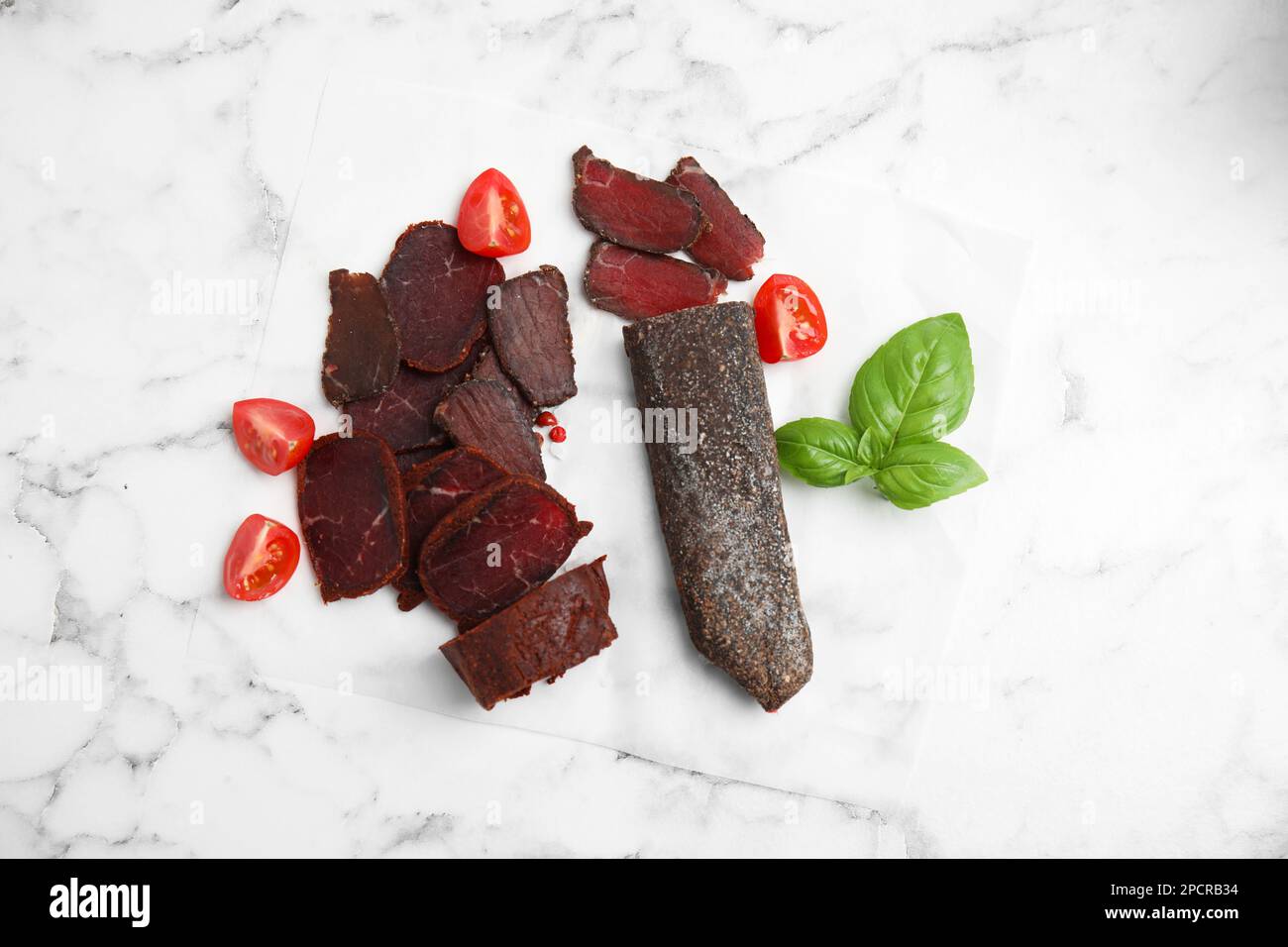 Delicious dry-cured beef basturma with basil and tomatoes on white ...