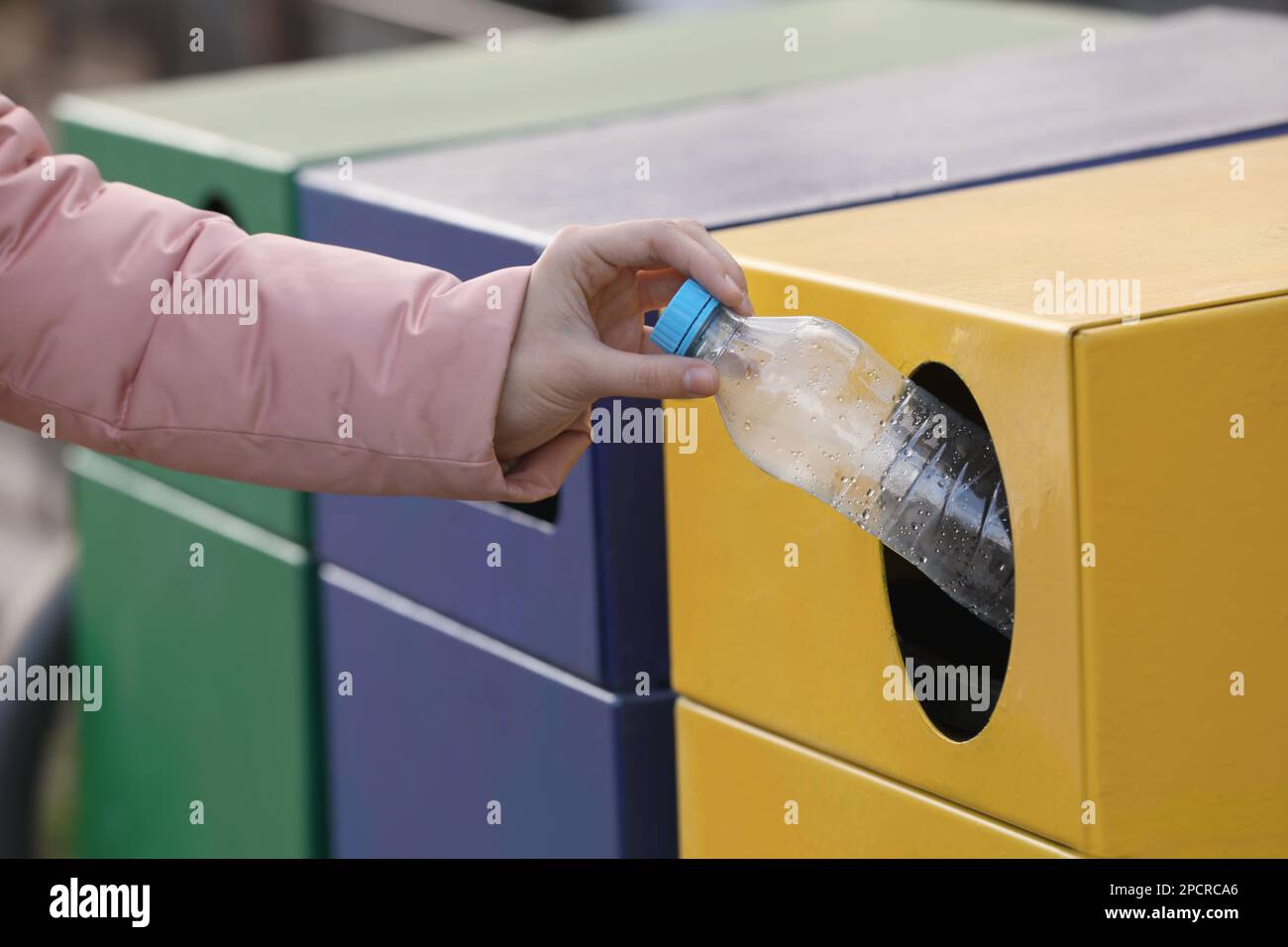 Woman throwing plastic bottle into garbage bin outdoors, closeup. Waste ...