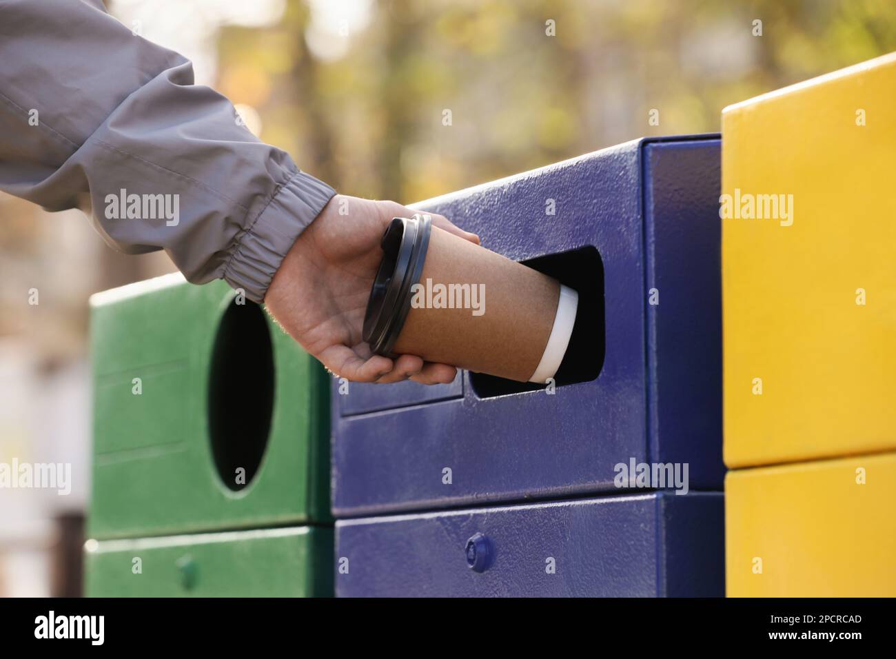 Man throwing paper coffee cup into garbage bin outdoors, closeup. Waste ...