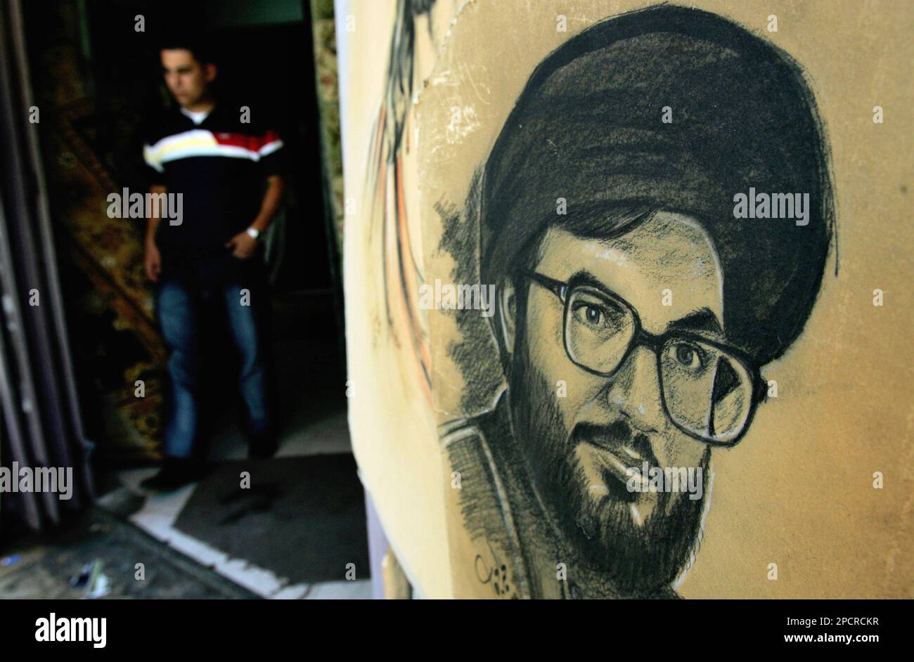 A Palestinian man stands next to a drawing depicting Hezbollah leader ...