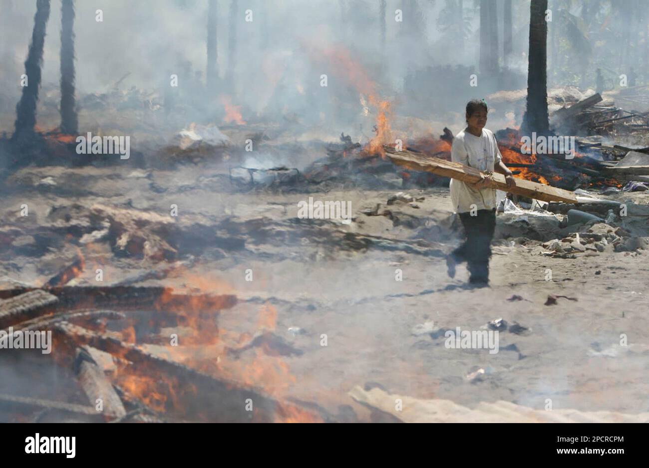 A tsunami survivor burns debris at a tsunami-ravaged village in ...