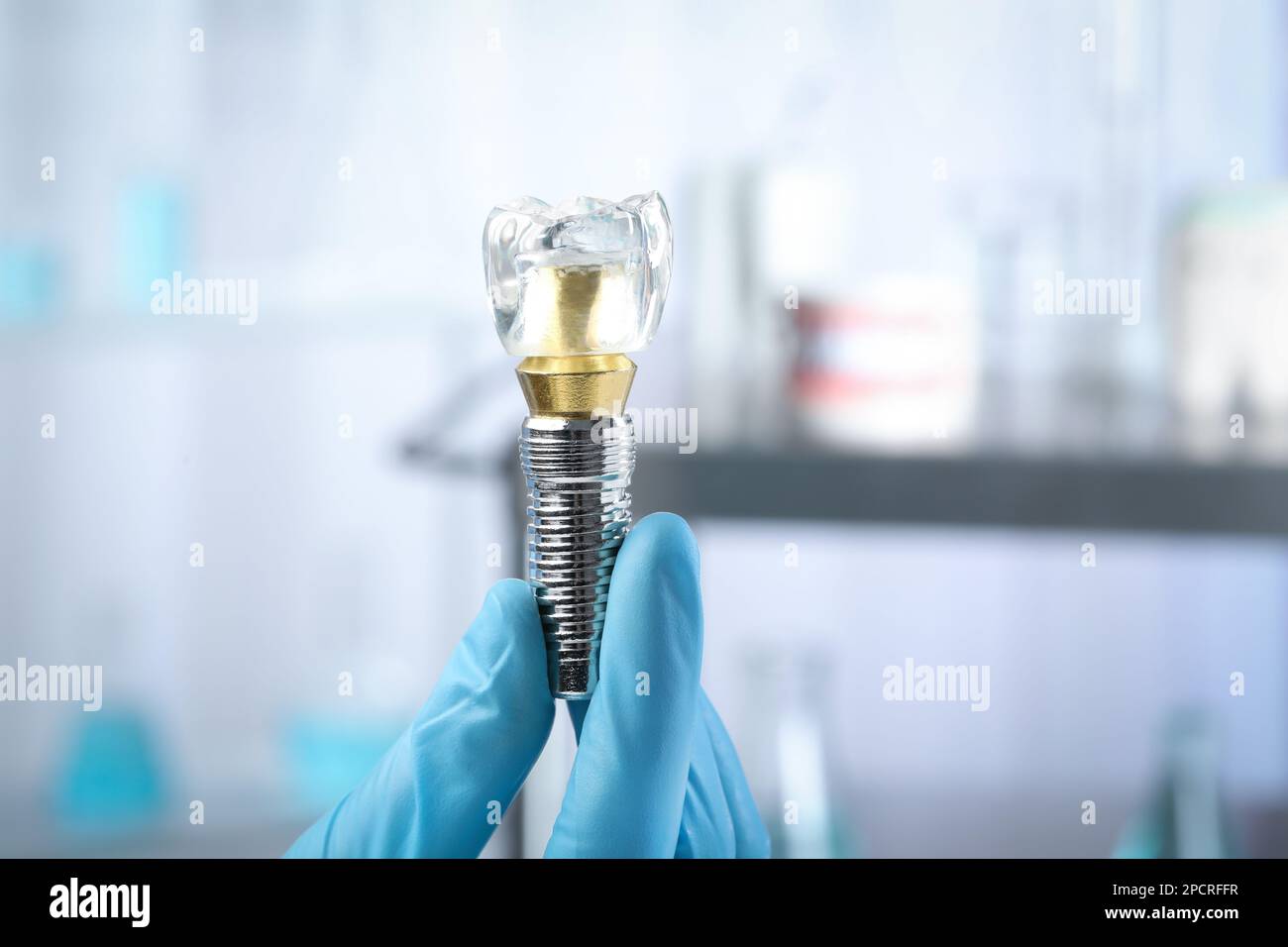 Dentist holding educational model of dental implant on blurred ...