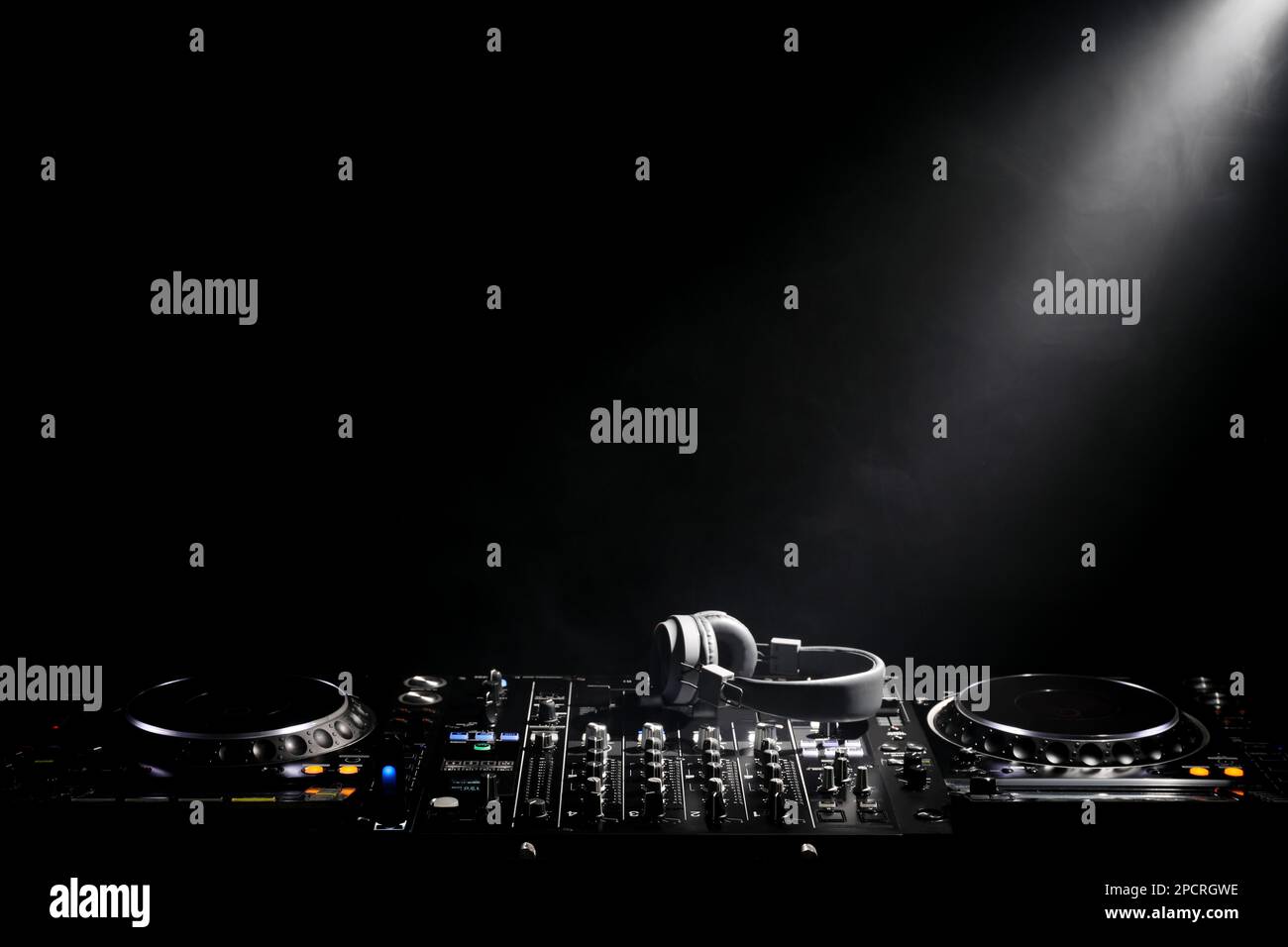 Modern DJ controller and headphones under beam of light on black ...