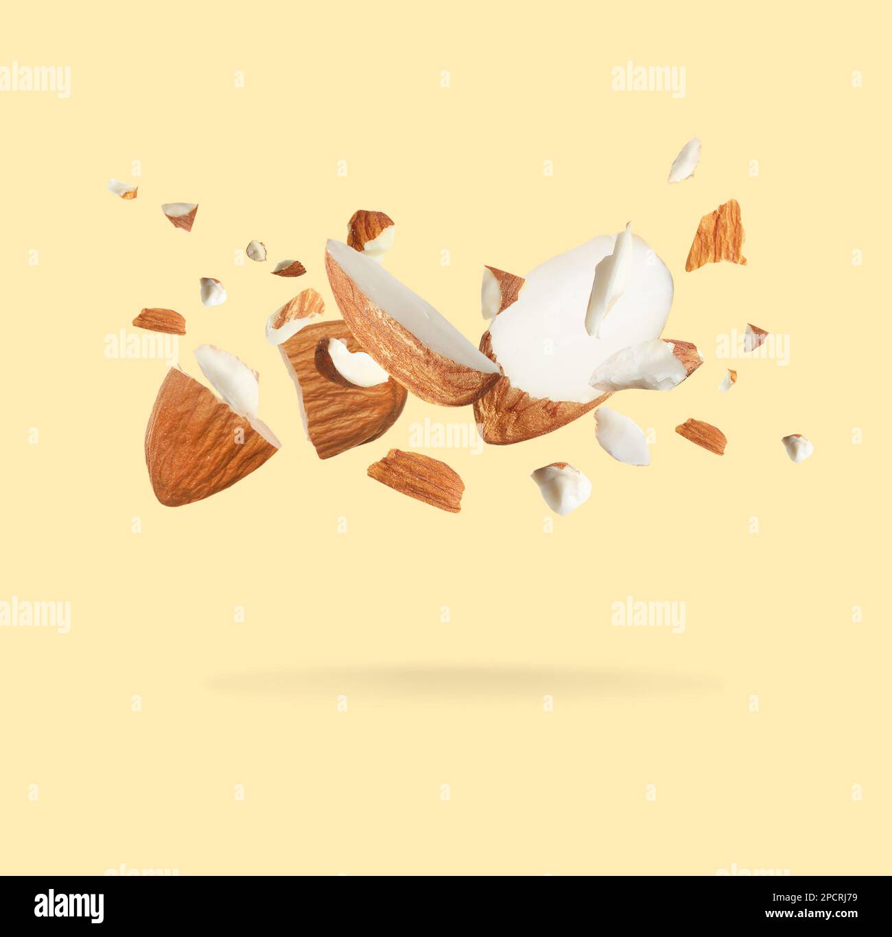 Pieces of tasty almonds falling on beige background Stock Photo - Alamy