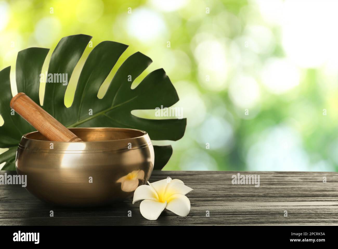 Golden singing bowl, mallet, green leaf and flower on wooden table ...