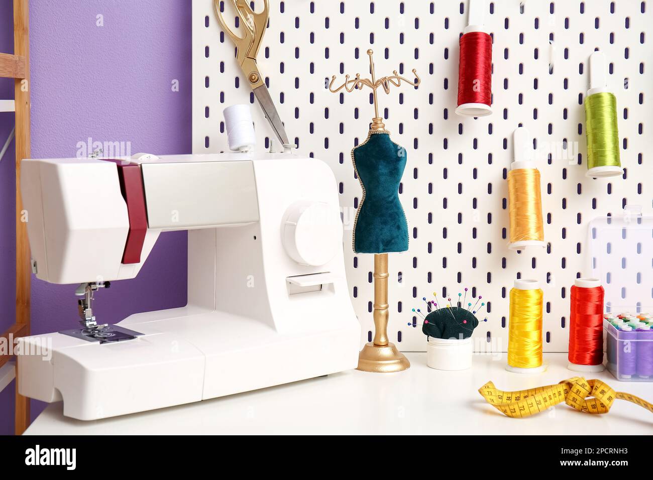 Sewing machine, mannequin and pegboard with thread spools on table in ...