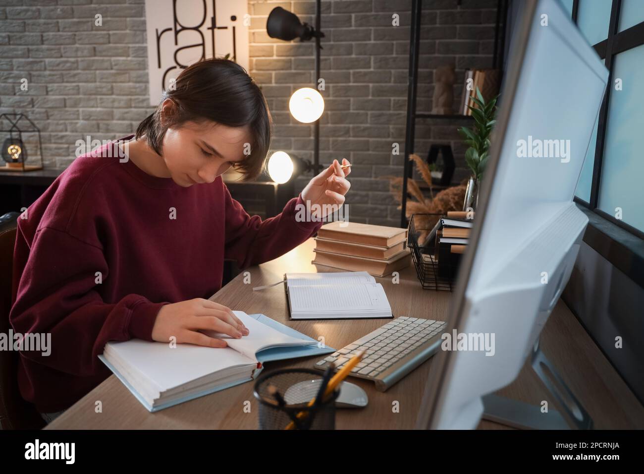 Teenage boy taking notes while reading book at table late in evening ...