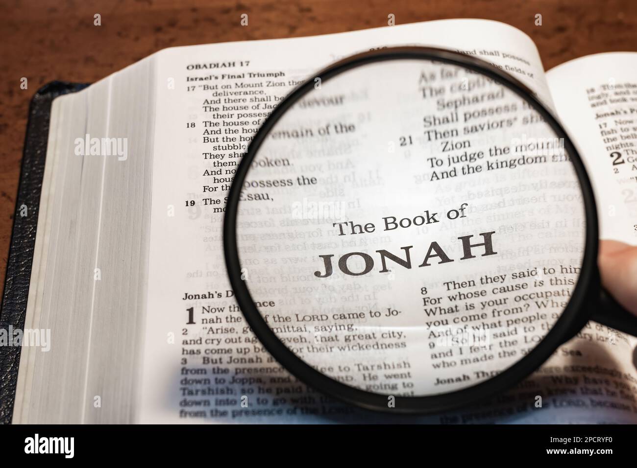 A closeup of a person holding a magnifier and reading the book of Jonah ...