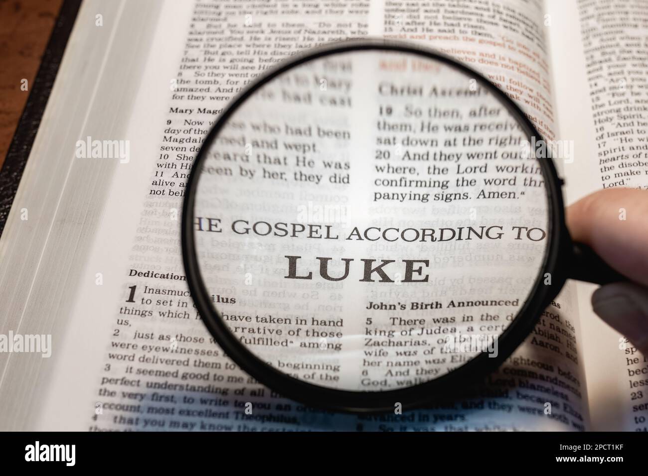 A closeup of a person holding a magnifier and reading the book of Luke ...