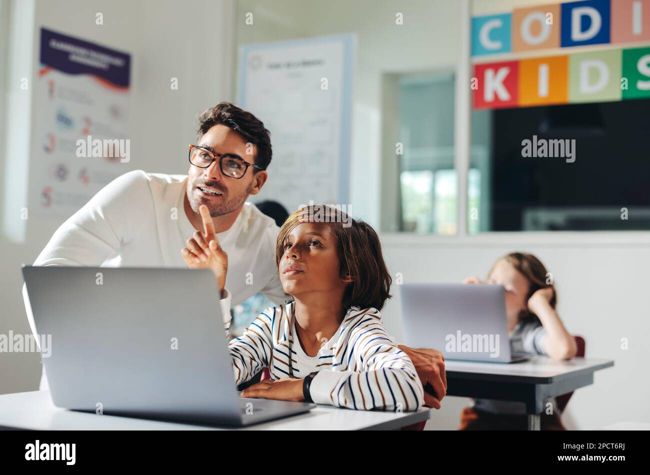 Teacher helping a young student understand a coding exercise in a class ...