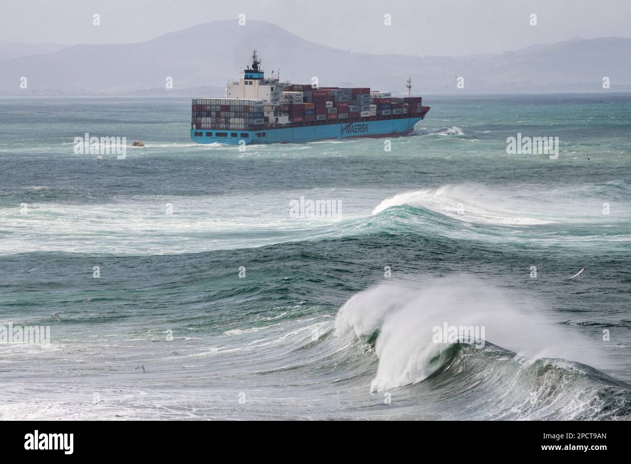 A giant cargo ship sailing across the rough pacific ocean with waves ...
