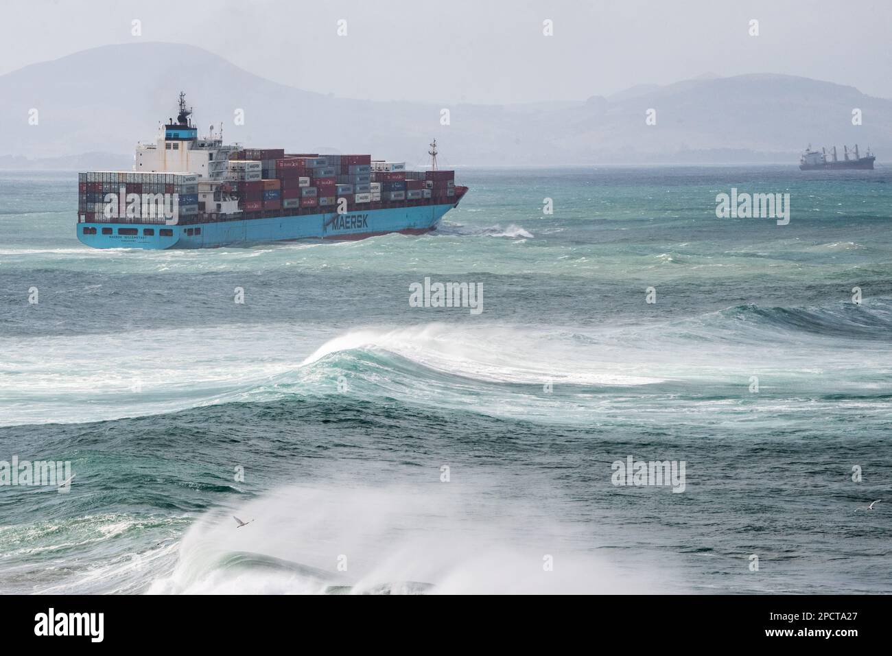A giant cargo ship sailing across the rough pacific ocean with waves ...