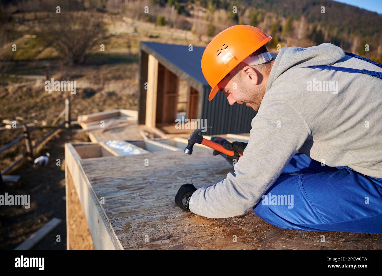 Carpenter hammering nail into OSB panel on the roof top of future ...