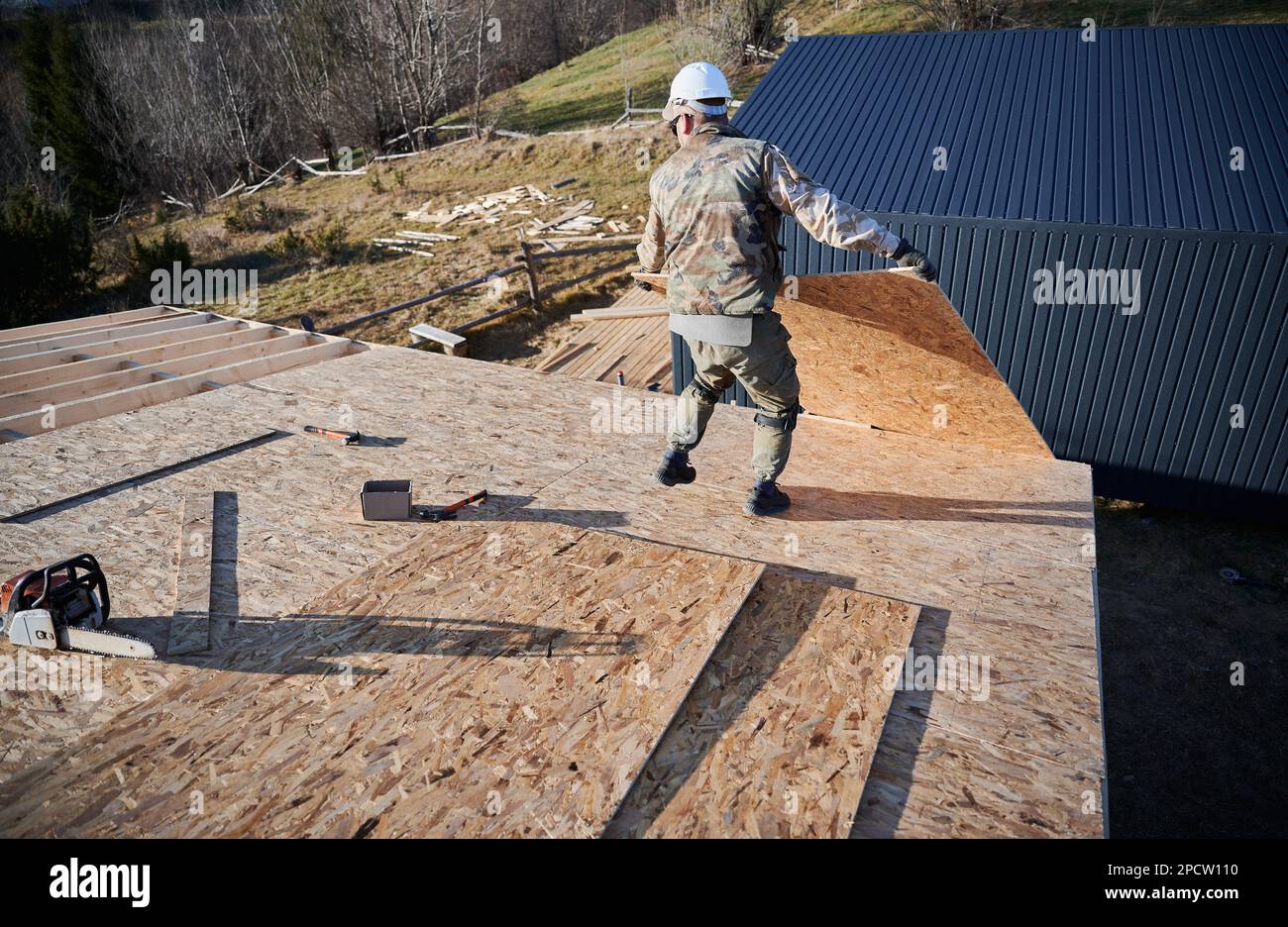 Carpenter mounting wooden OSB panel on rooftop of future cottage. Man ...