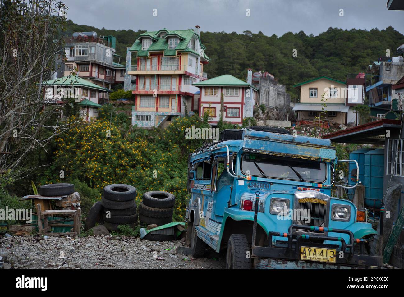 An old blue bus with colorful huts and a forest in the background in ...