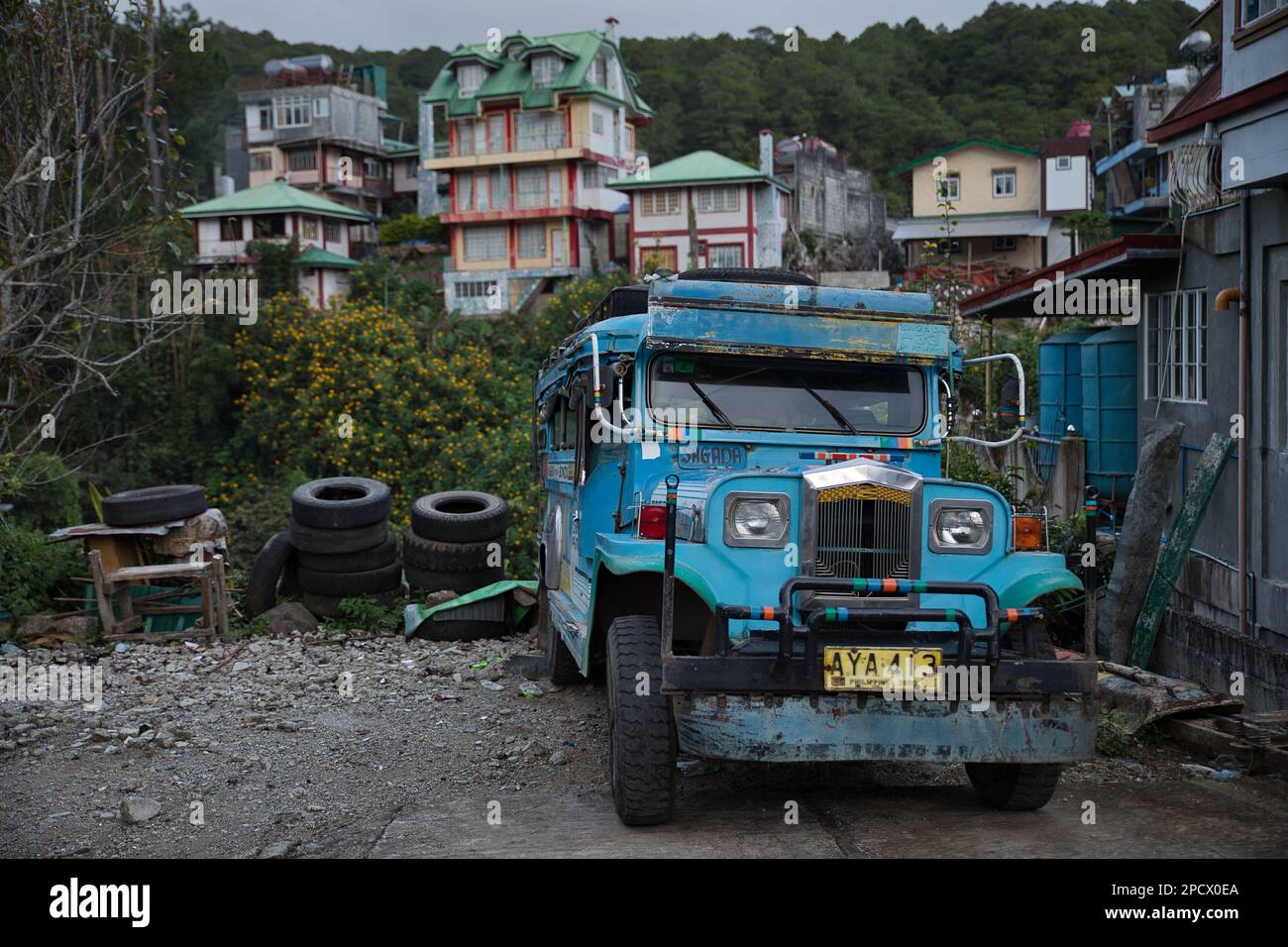 An old blue bus with colorful huts and a forest in the background in ...