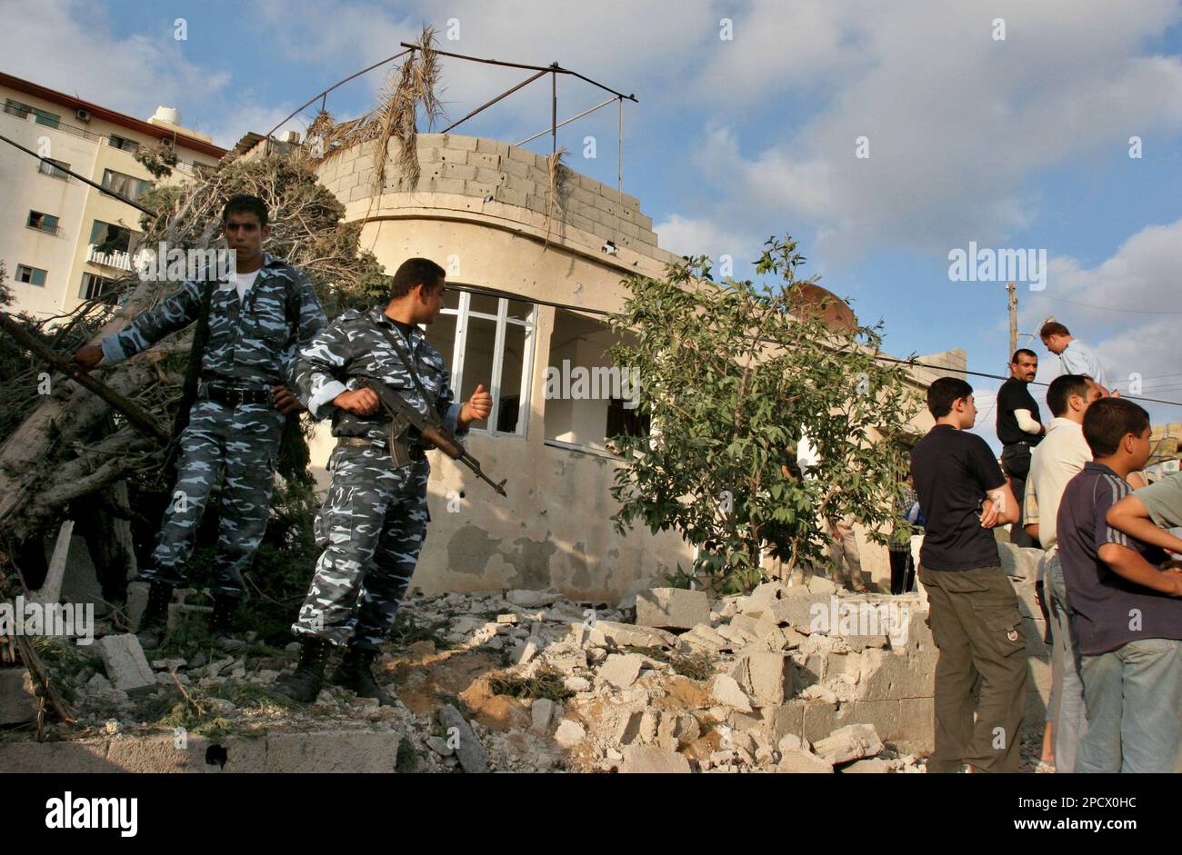 Palestinians look at the wreckage of a car as they stand in the rubble ...