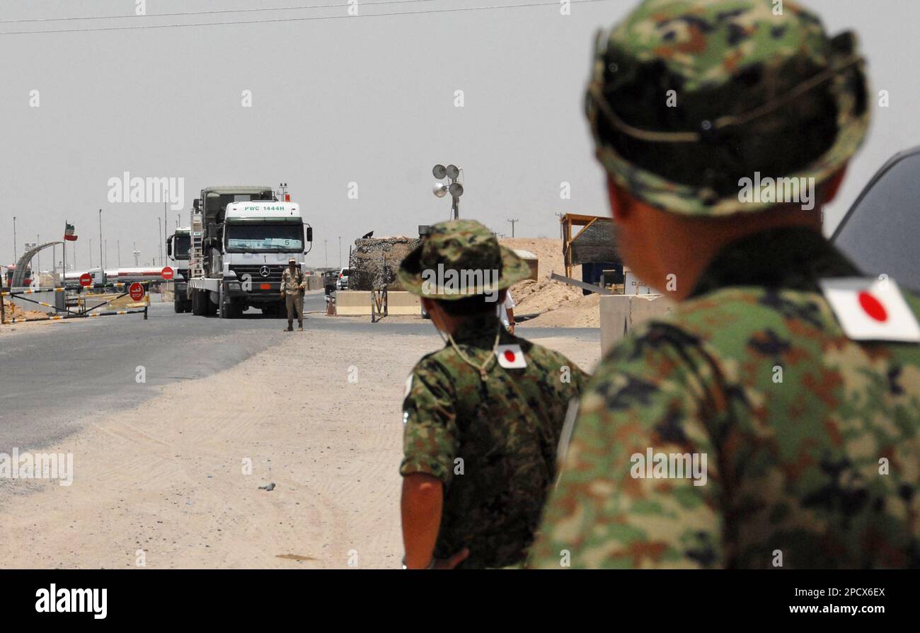 Two Japanese Self Defense Forces soldiers watch a convoy of withdrawing ...