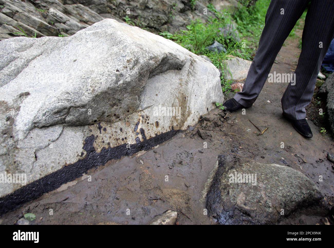 A villager stands near a line of coal tar sludge left after a spill of ...