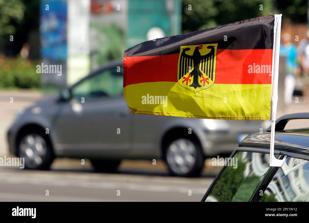 A German flag mounted on the top of a car blows in the wind in downtown ...