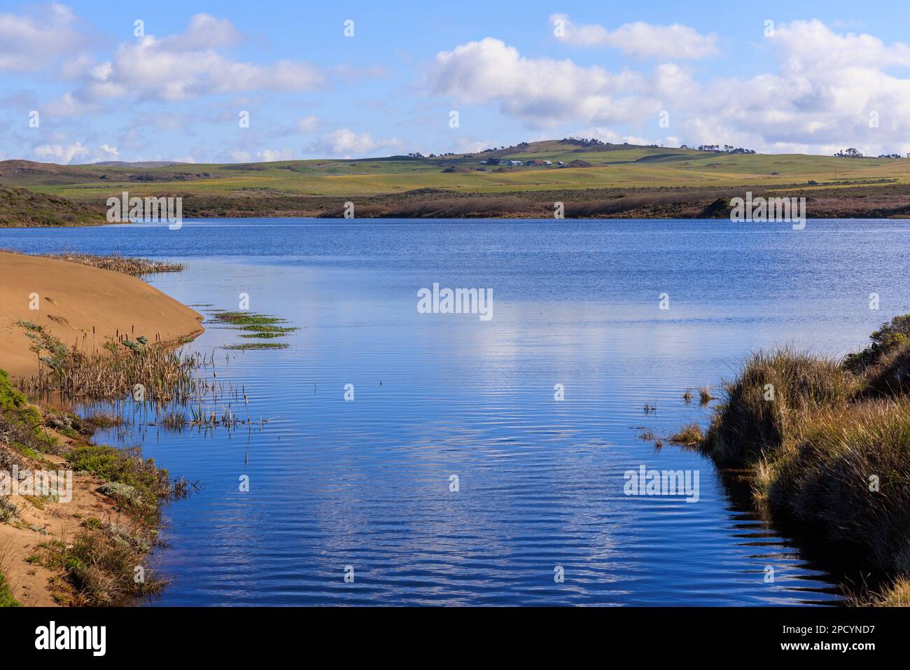 Calm blue waters in coastal lagoon with rolling green hills in ...