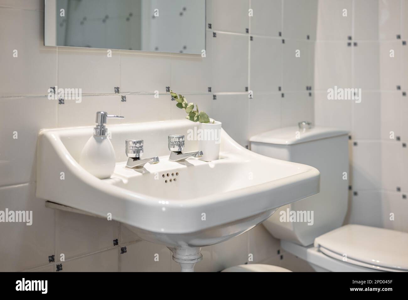 Bathroom with white tiled toilet bowl and sink with two taps and mirror ...