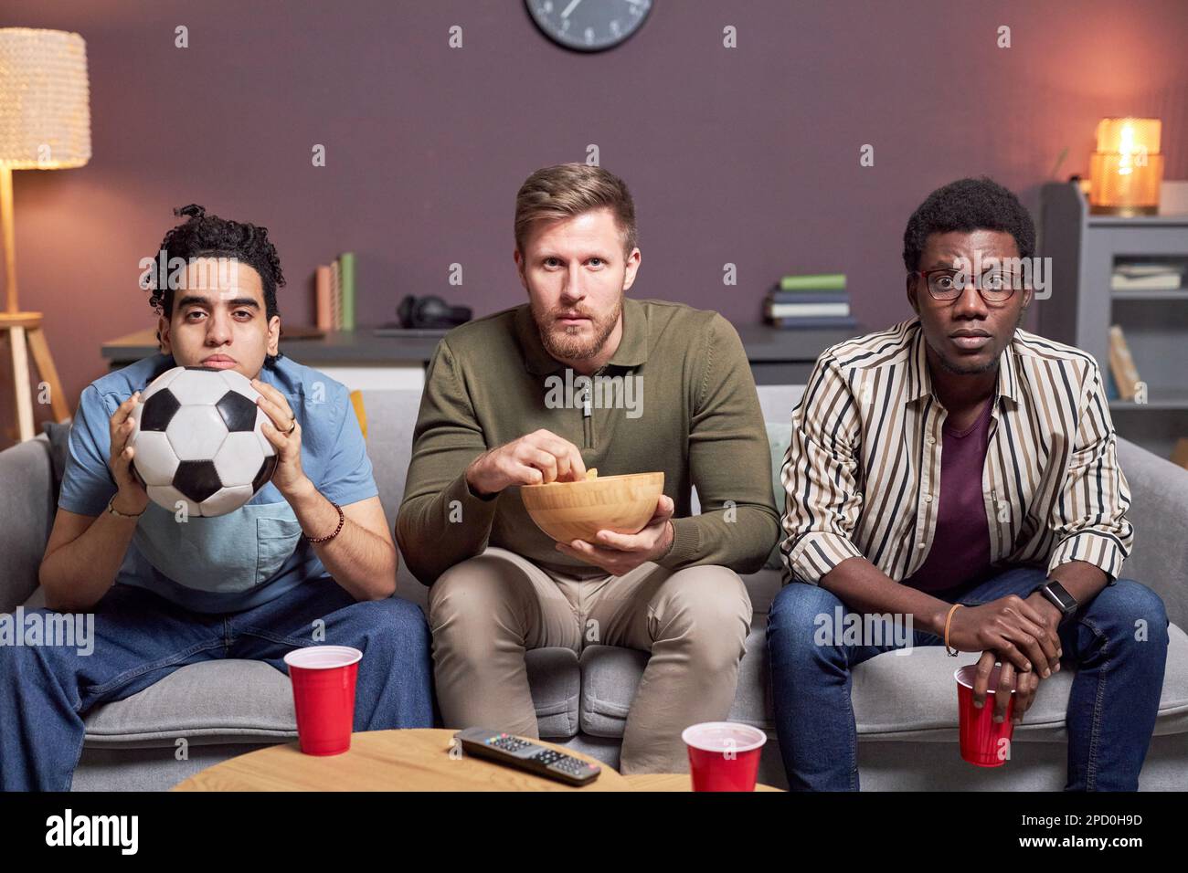 Front view at group of fans watching sports match at home with intense ...