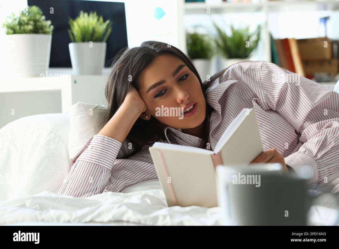 Beautiful woman lies in bed and reads book Stock Photo - Alamy
