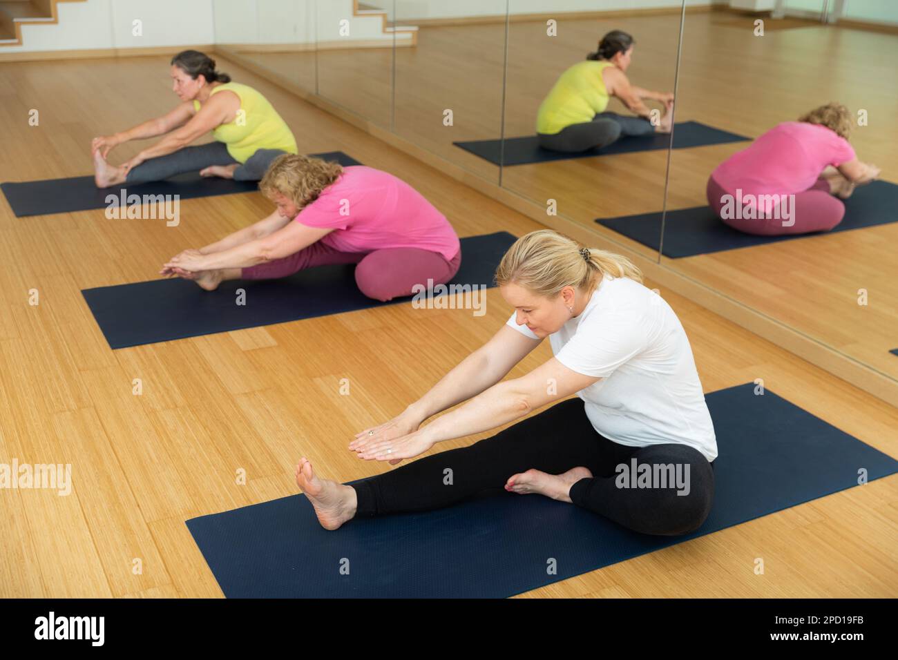 Women practicing yoga, sitting in Seated forward bend exercise ...