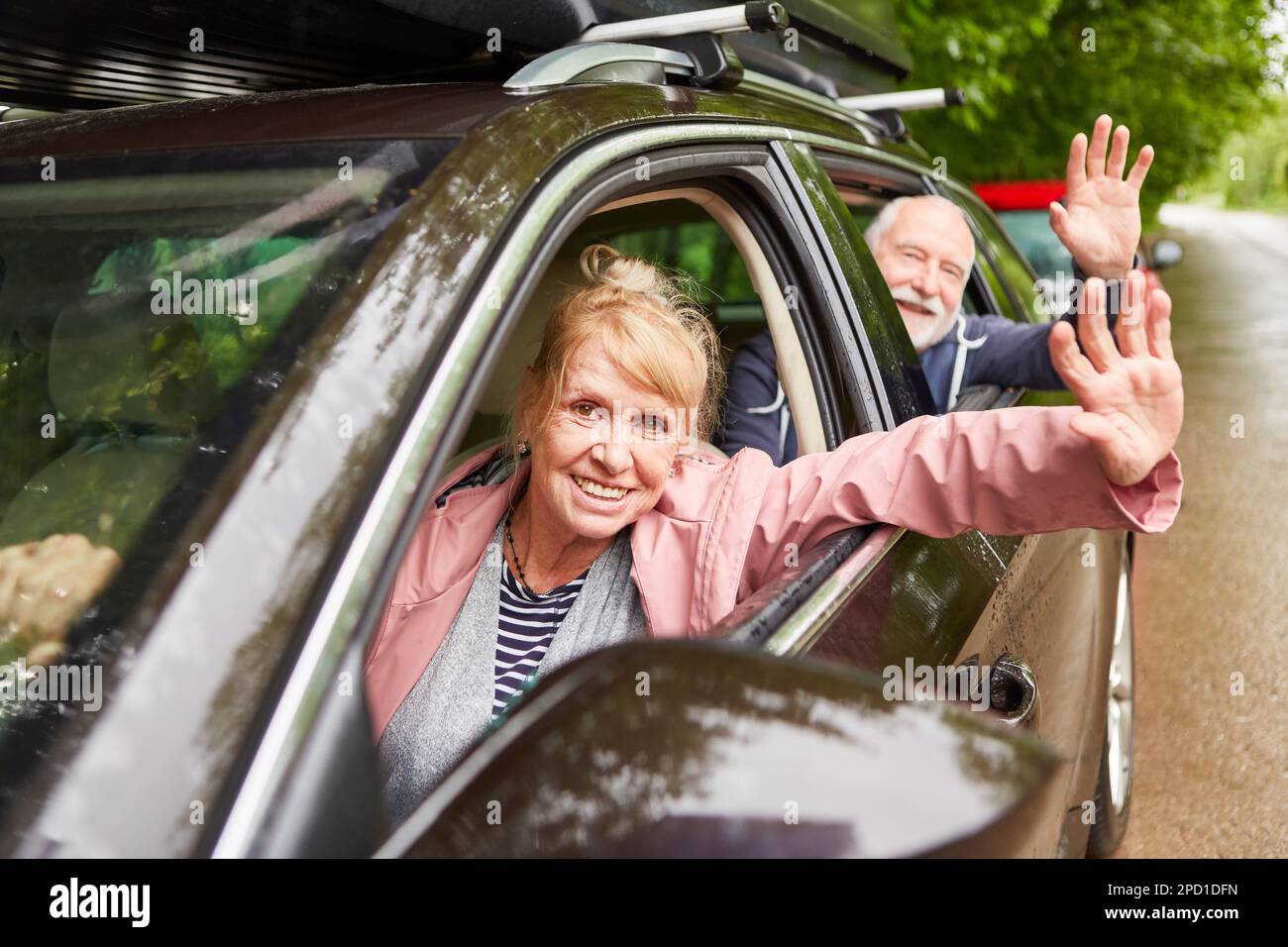 Portrait of happy senior couple waving hands through windows while ...