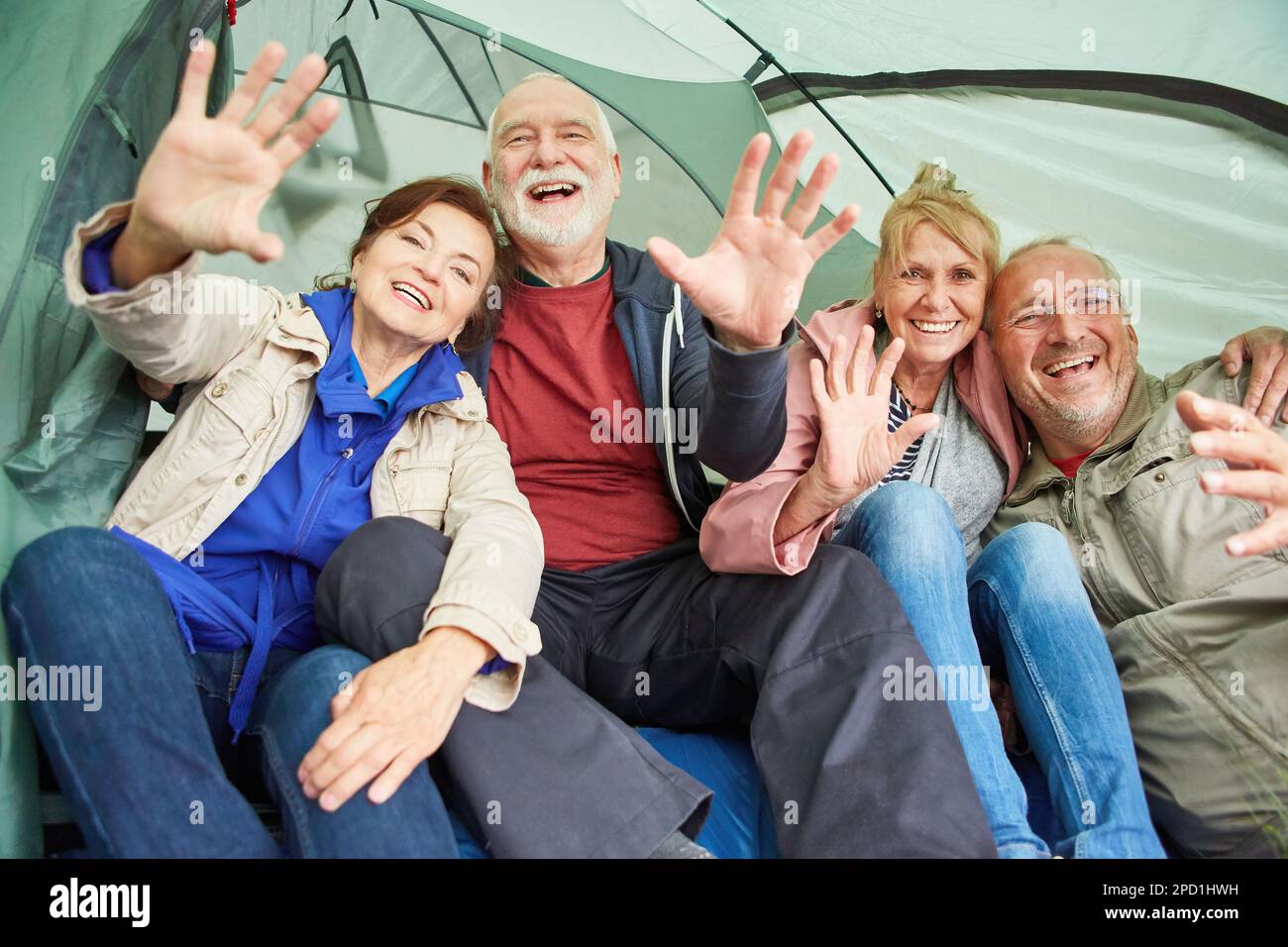 Portrait of cheerful senior couples waving while sitting in tent at ...