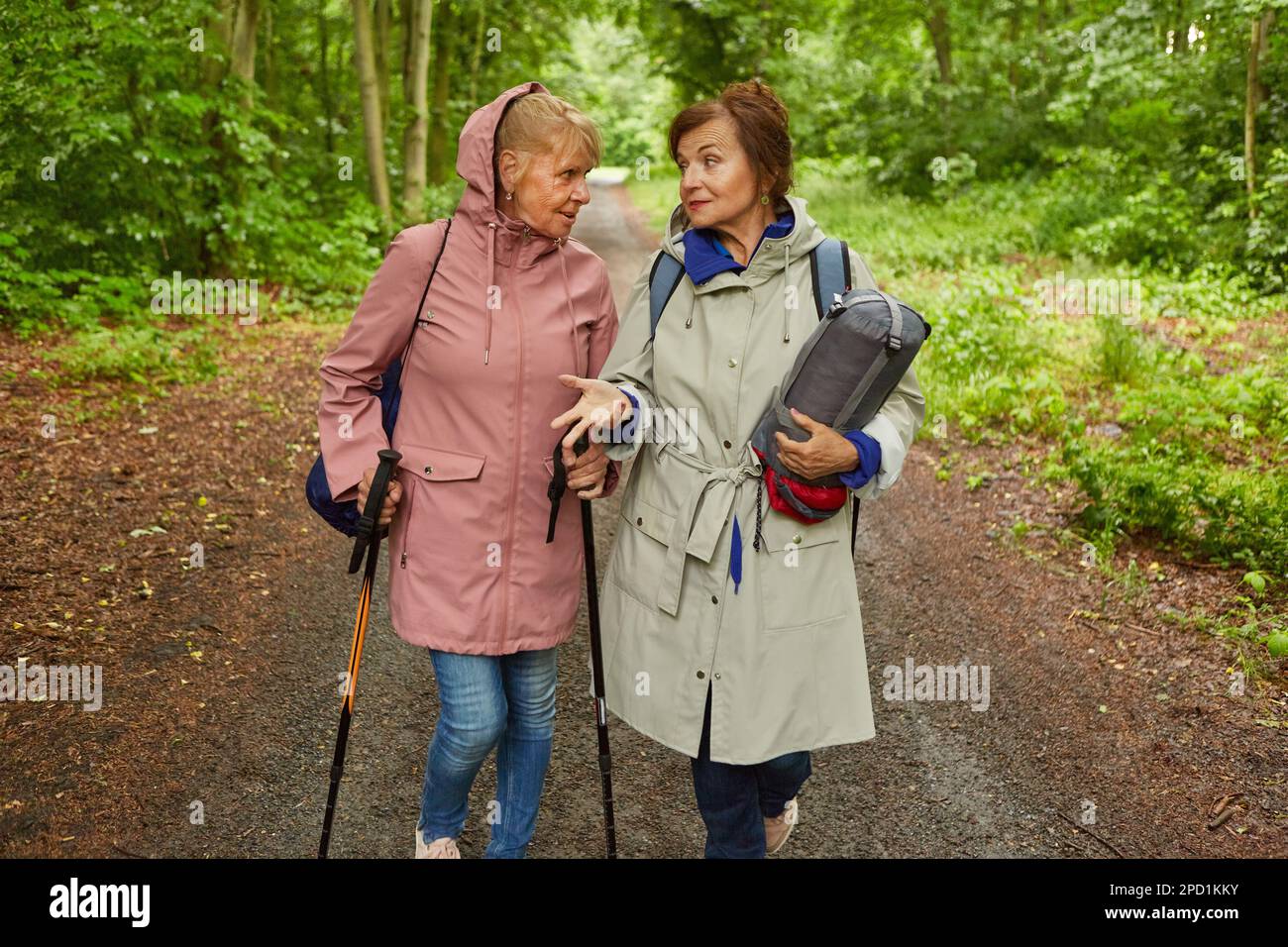 Senior woman talking with female friend while hiking on path in forest ...