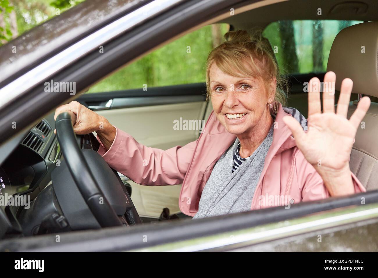 Portrait of smiling elderly woman waving hand through window while ...