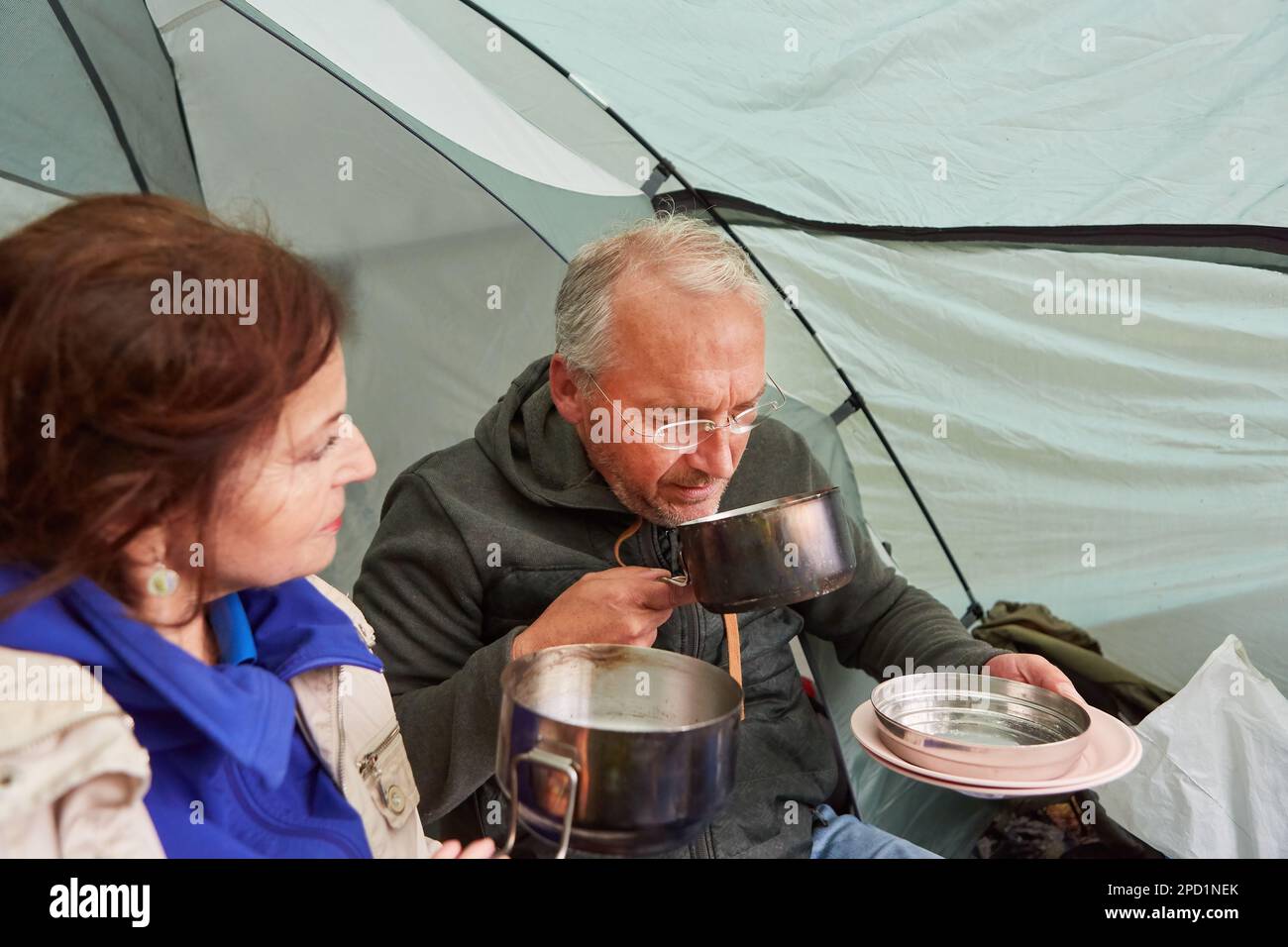 Elderly man smelling food sitting by woman in camping tent during ...