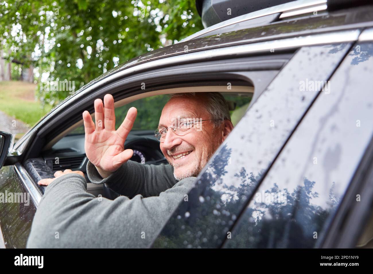 Portrait of happy senior man waving hand through window while driving ...