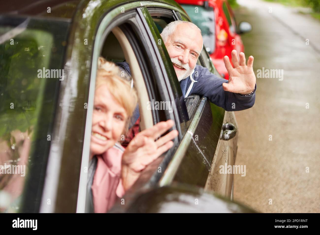 Portrait of happy elderly couple waving hands through windows while ...