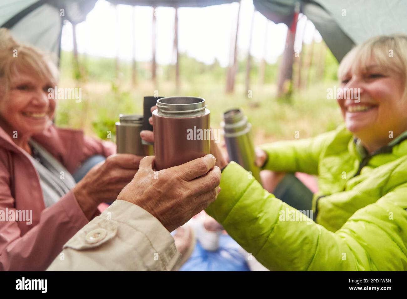 Elderly women enjoys toasting tea cups while camping in forest during ...