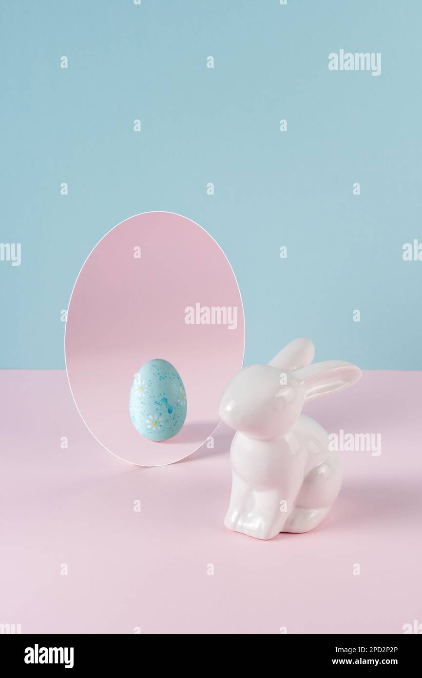 Creative concept with Easter bunny and egg in mirror on pastel pink ...