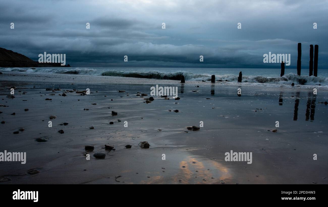 A wet sandy beach with sea water and some logs on the sand in South ...