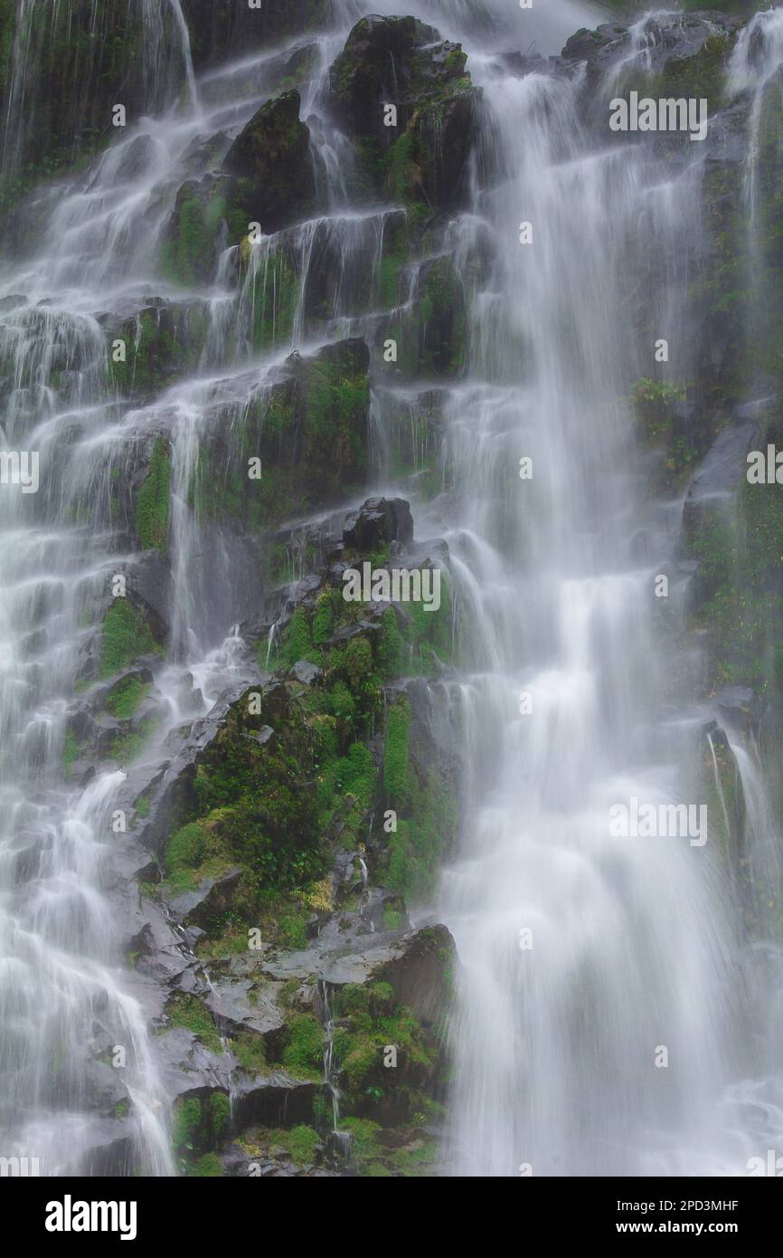 A natural waterfall flows down a long line from a cliff into a ...